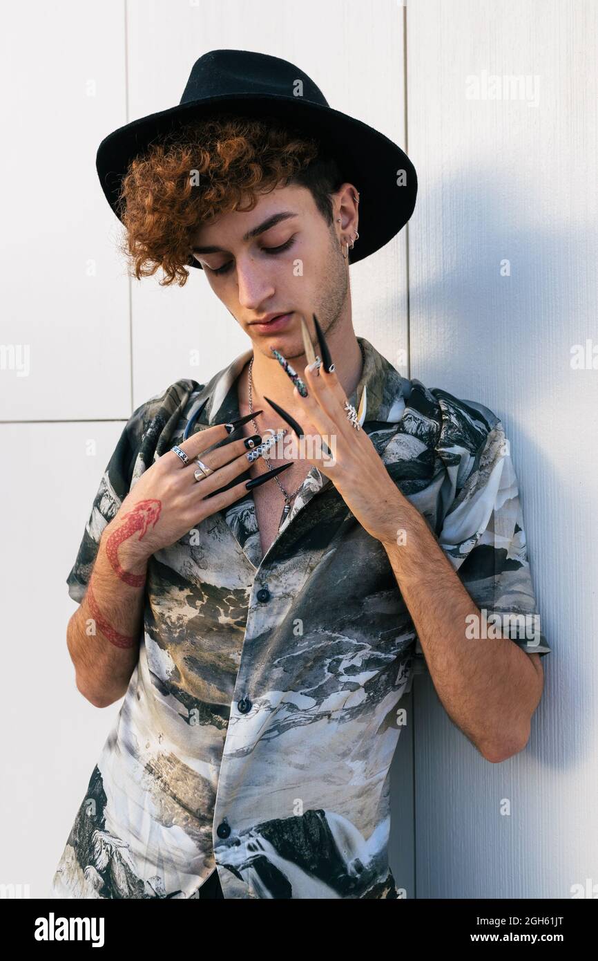 Young vain man in stylish wear with hat standing on tiled wall looking ...
