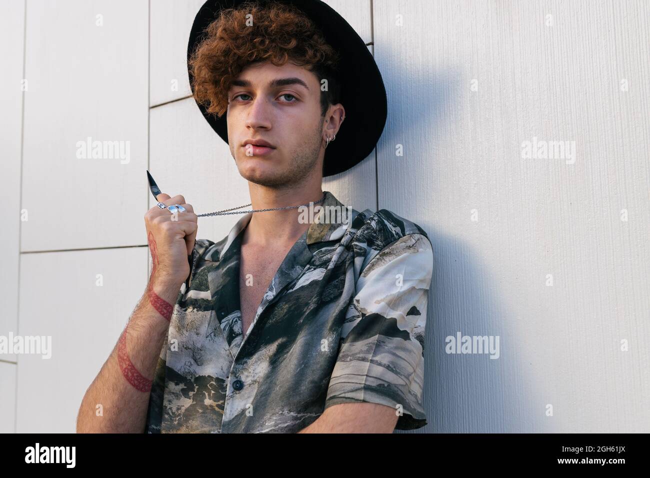 Young vain man in stylish wear with hat standing on tiled wall looking ...