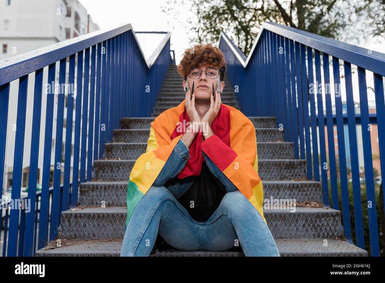 From below of stylish gay male with LGBT flag on shoulders sitting on ...