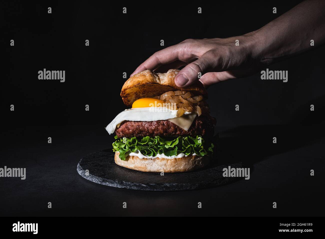 Crop unrecognizable person putting bun on burger with egg and patty ...
