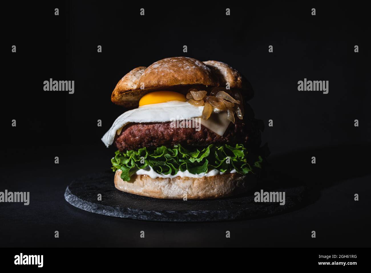 Tasty burger with egg placed on patty and fresh lettuce served on slate ...