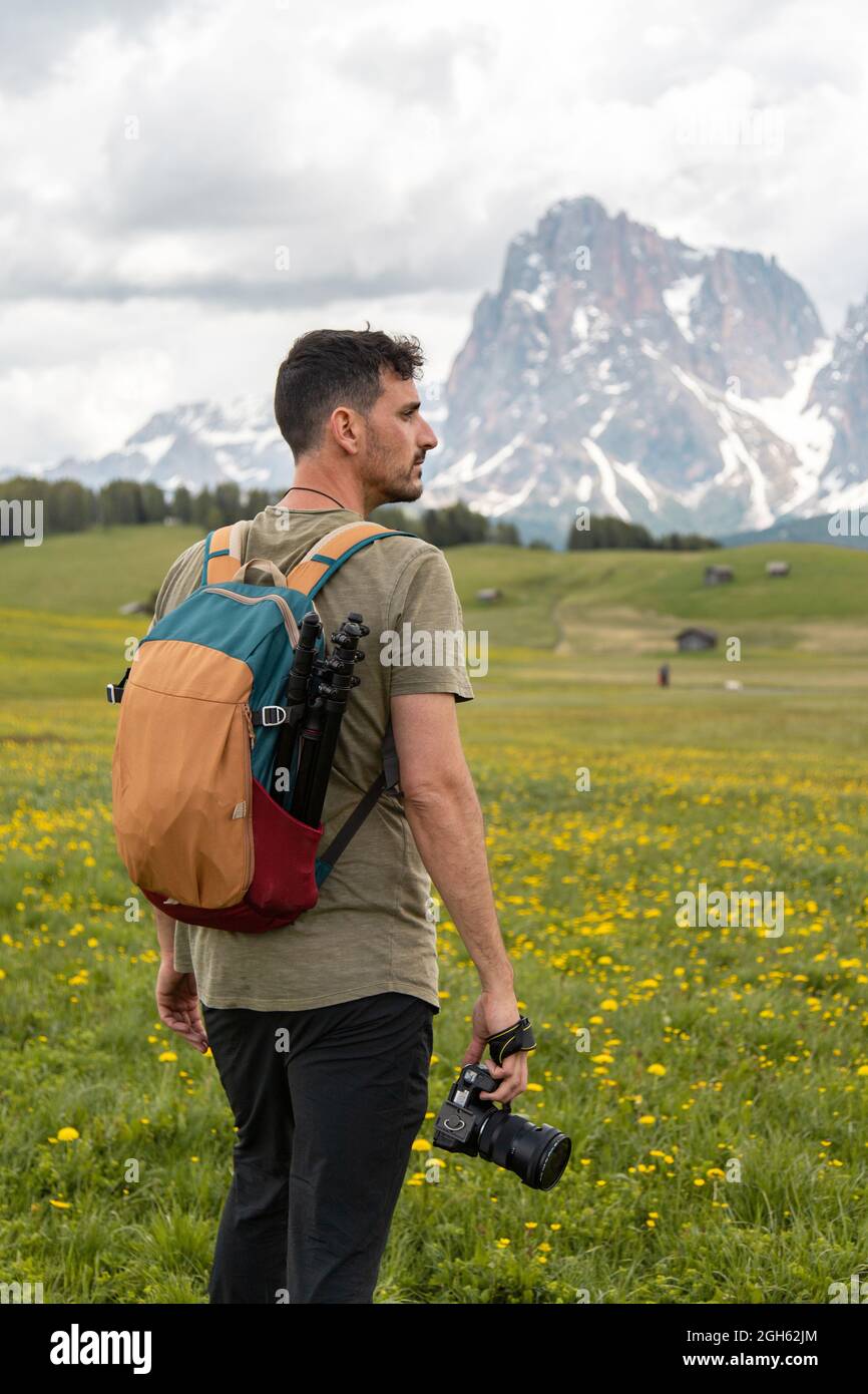 Back view of traveling male photographer with camera standing on meadow ...