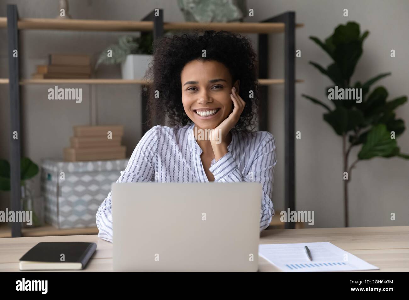 Mixed race female employee posing at work desk by laptop Stock Photo ...