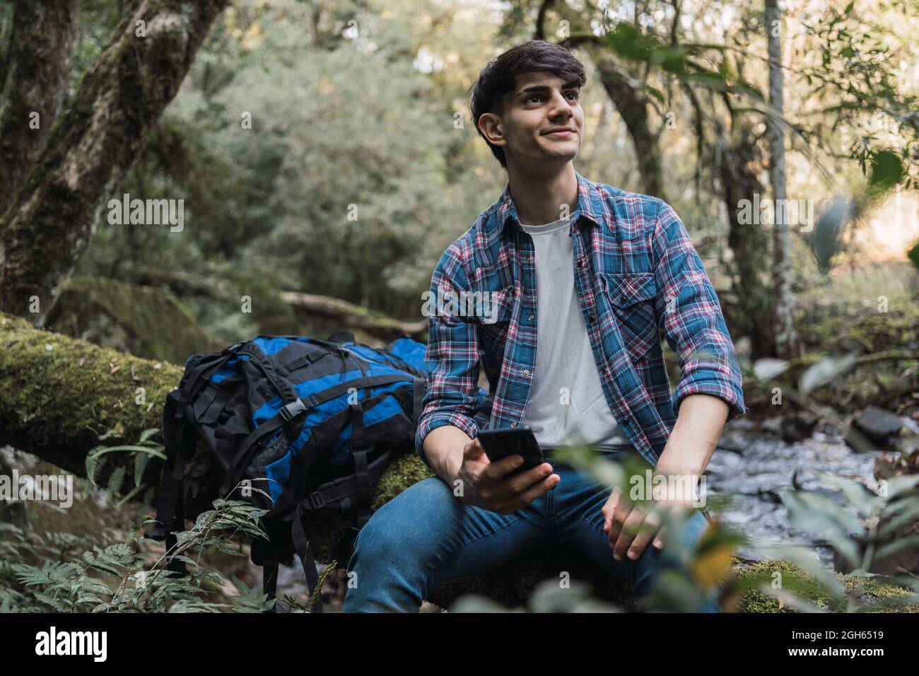 Side view of content male hiker with backpack sitting near lake in ...