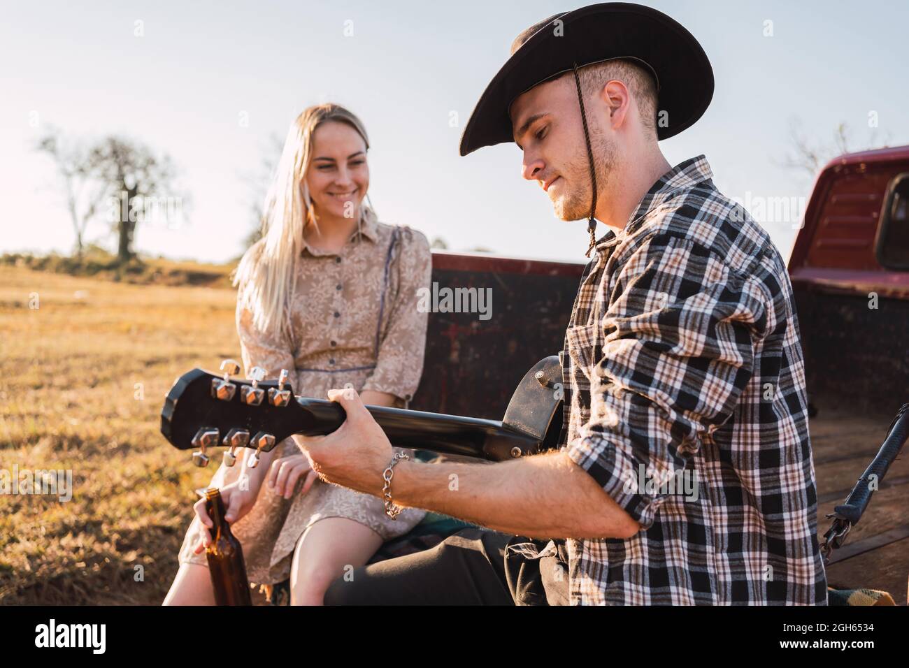 boyfriend in cowboy hat playing acoustic guitar while sitting with ...