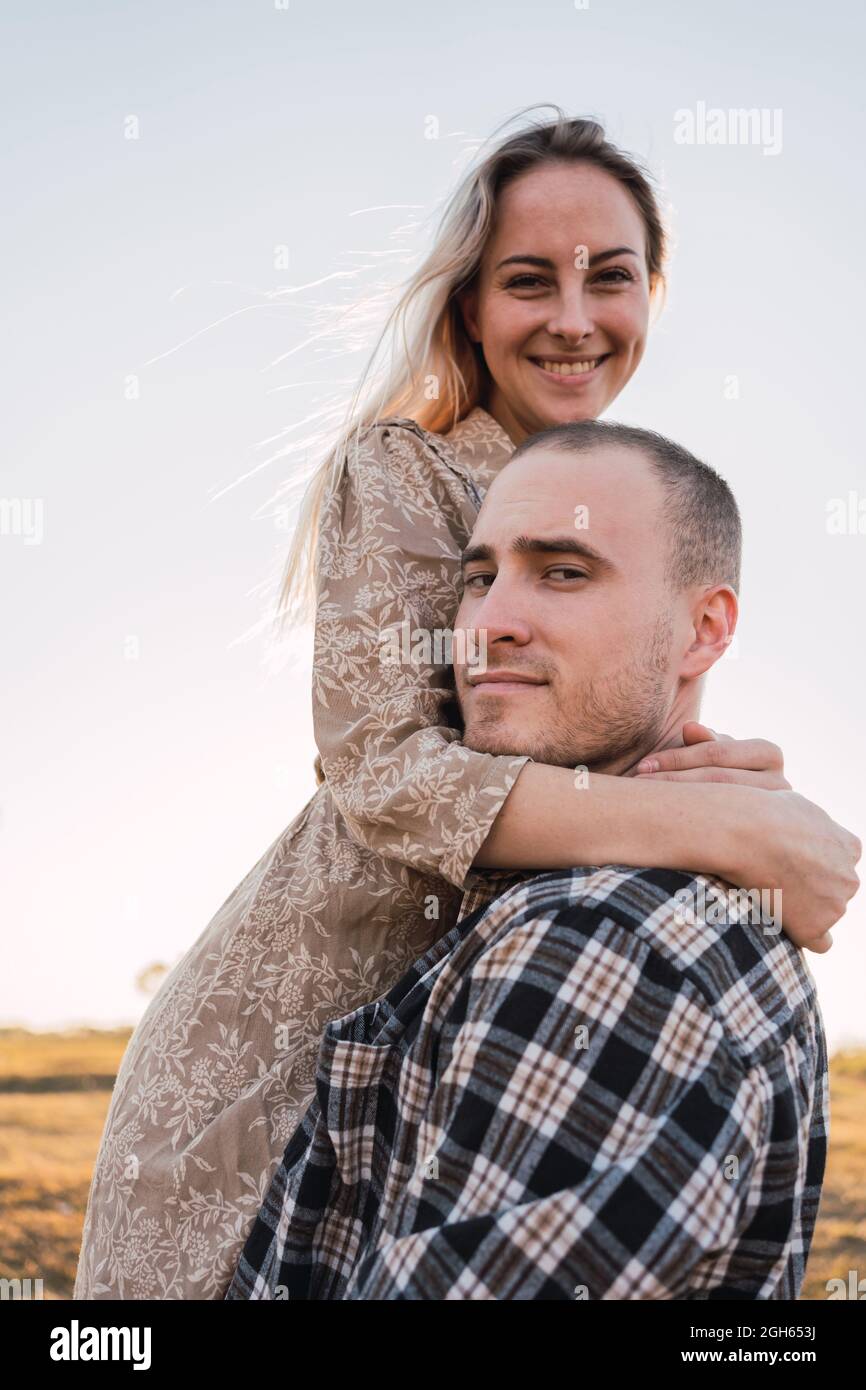 Cool boyfriend embracing smiling girlfriend while looking at camera ...