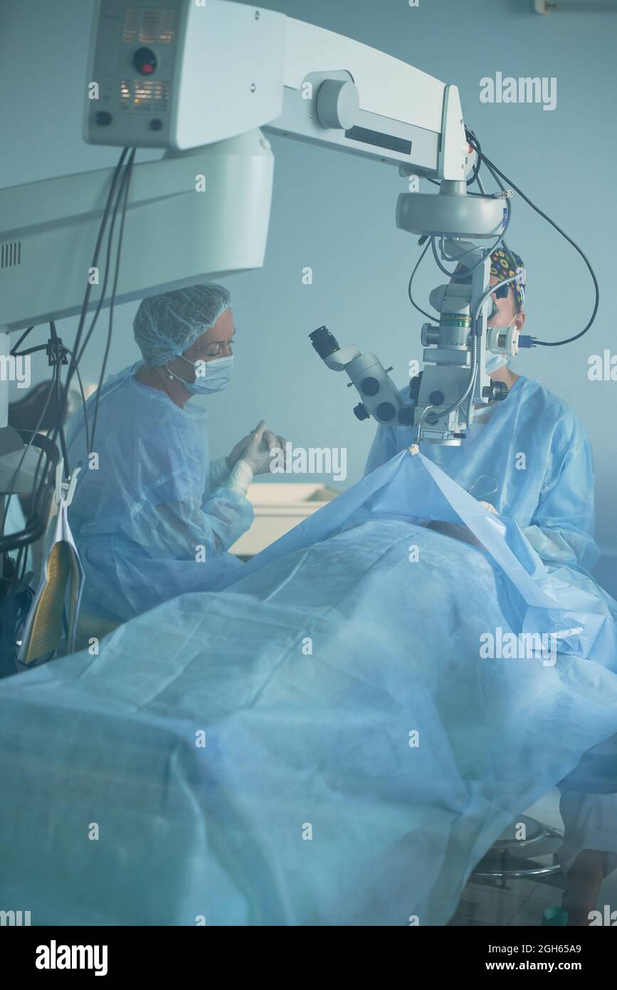 Anonymous doctor in sterile uniform looking through microscope over ...