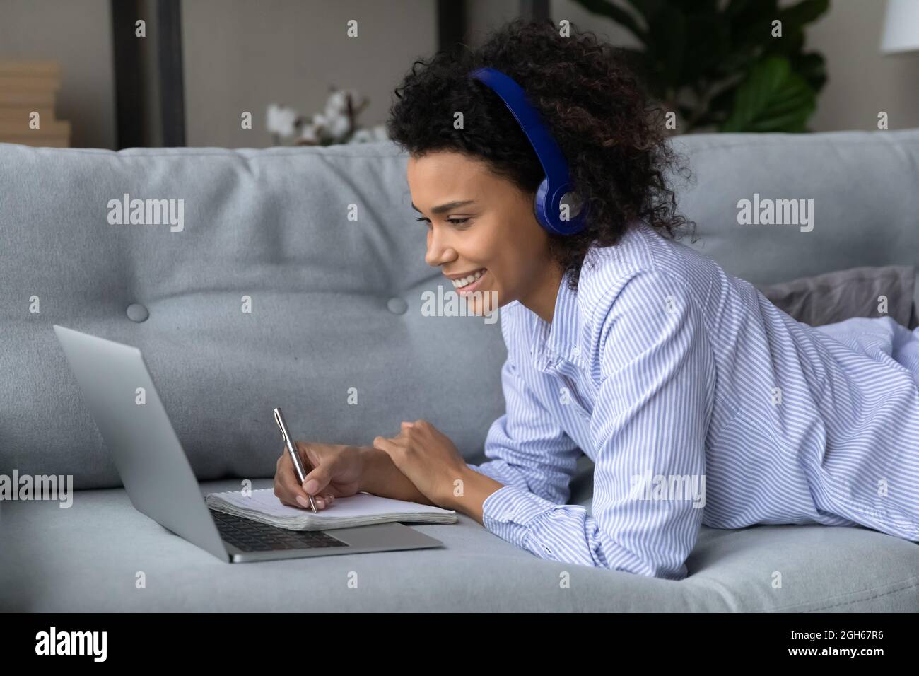 Black young female in earphones lying before laptop taking notes Stock ...