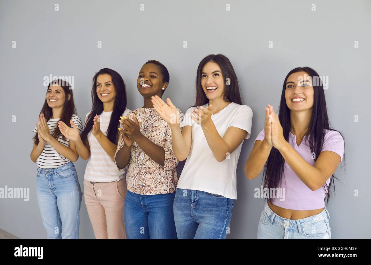 Group of happy young multiracial women standing by wall, clapping hands ...