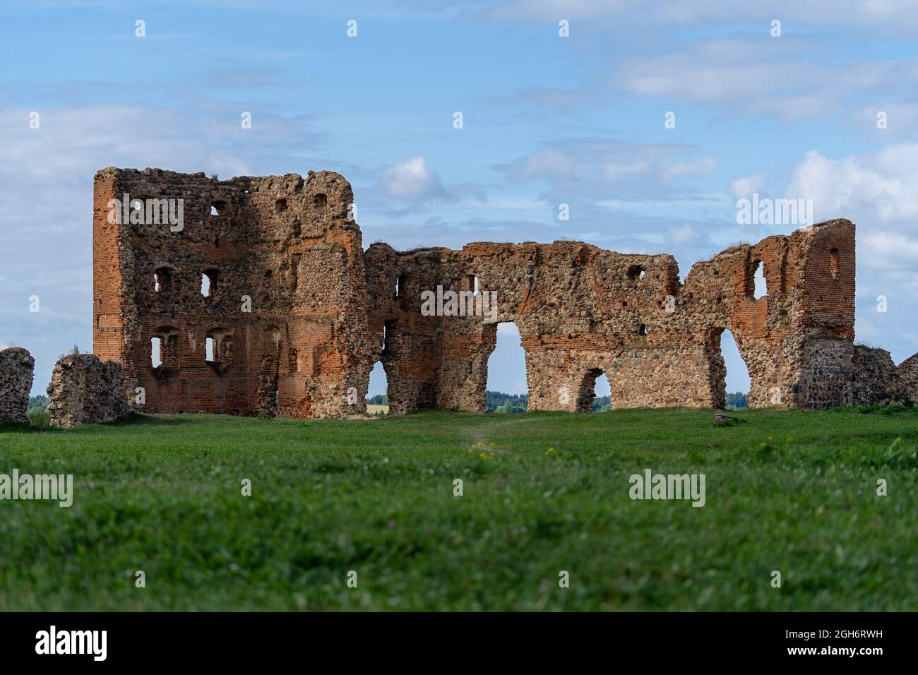 Remains of Ludza castle ruins on the foreground of green grass and blue ...