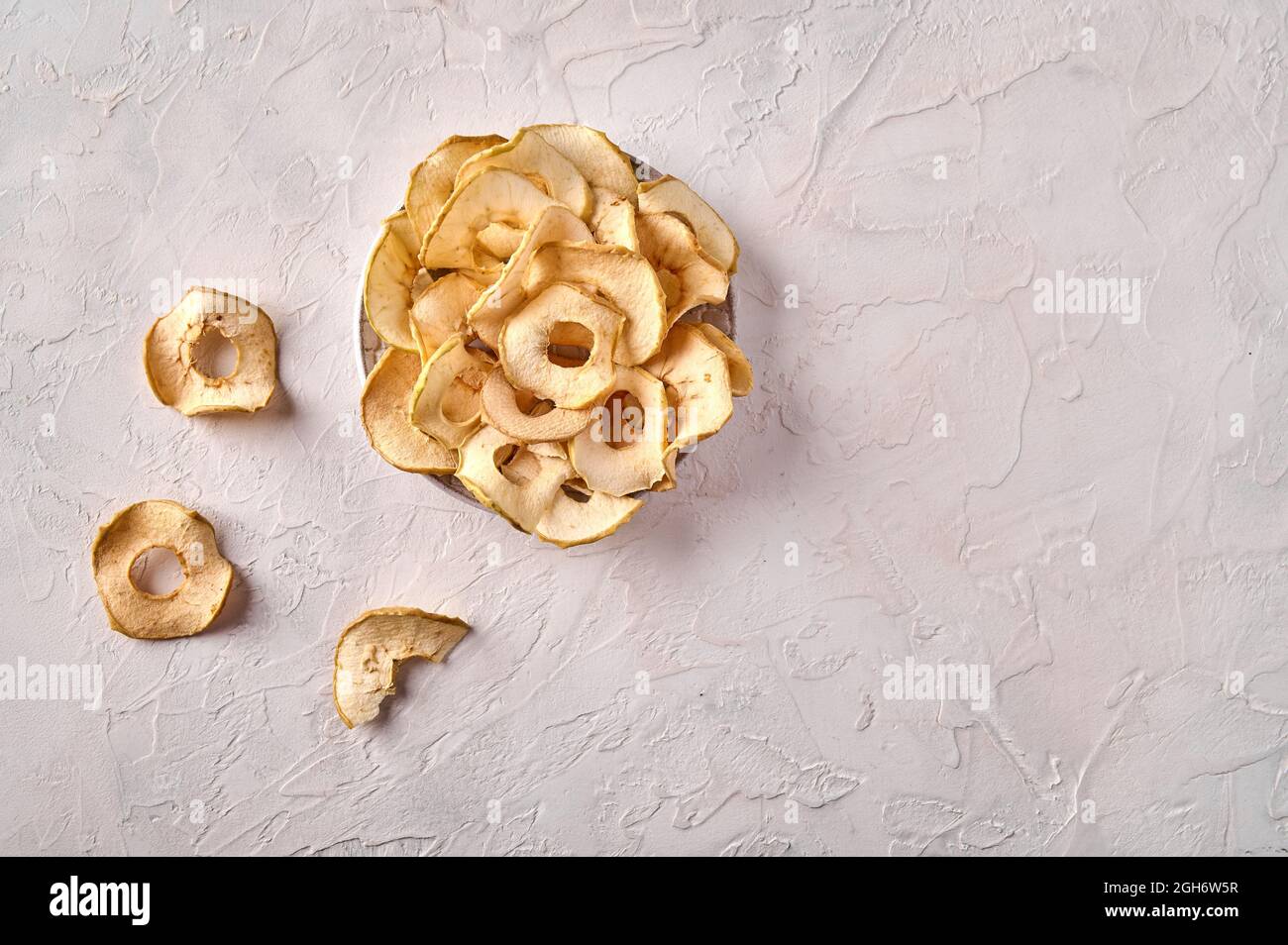 Dehydrated apples chips on plate on light wooden background. Top view ...