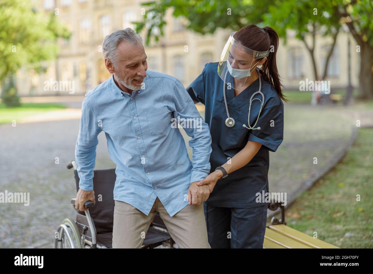 Supportive nurse wearing face shield and mask helping mature man ...