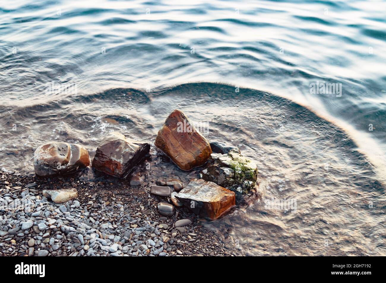 Boulders and rocks on sea shore washed with waves and causing ripples ...