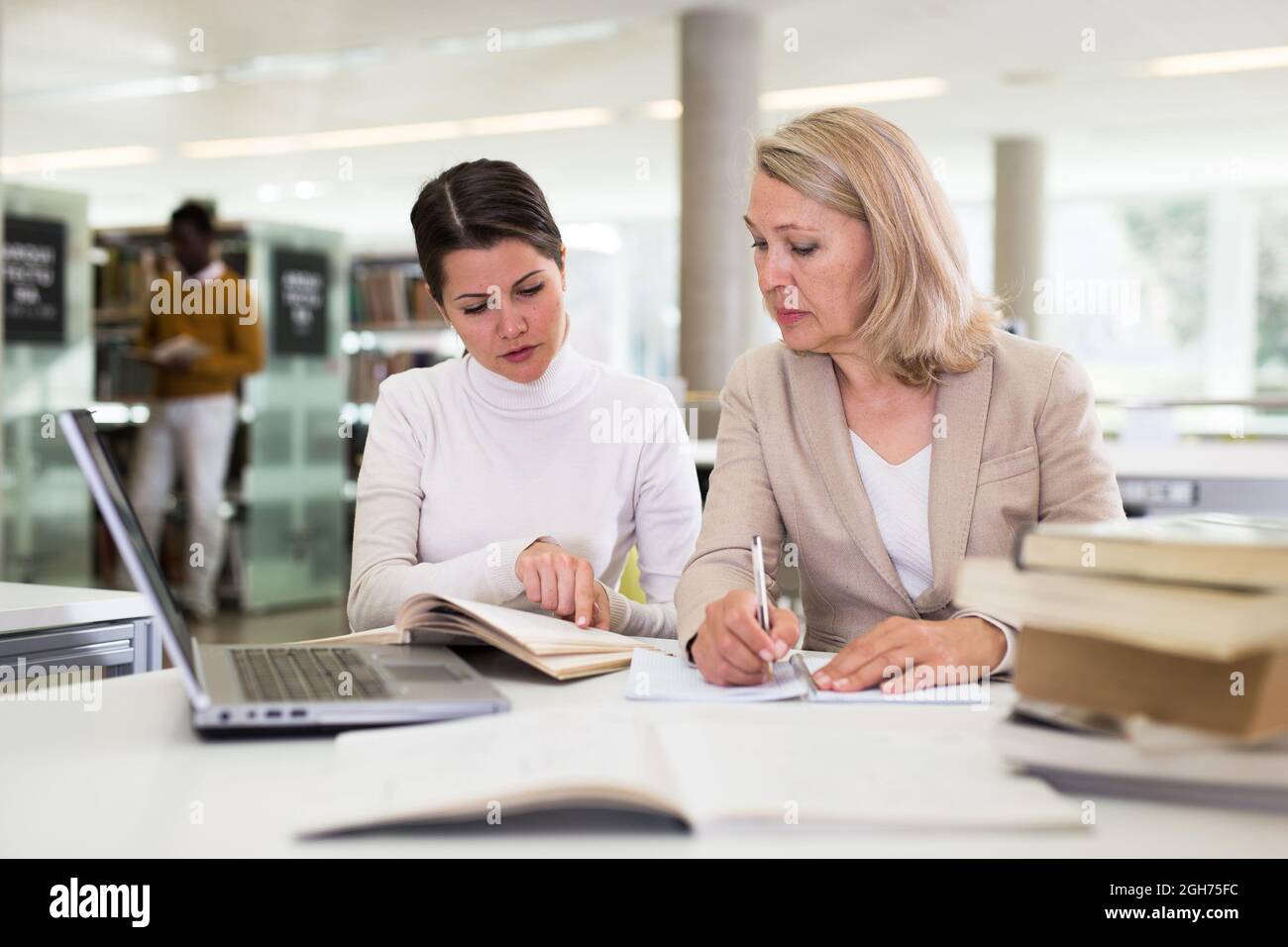 Female teacher working with girl student in university library Stock ...