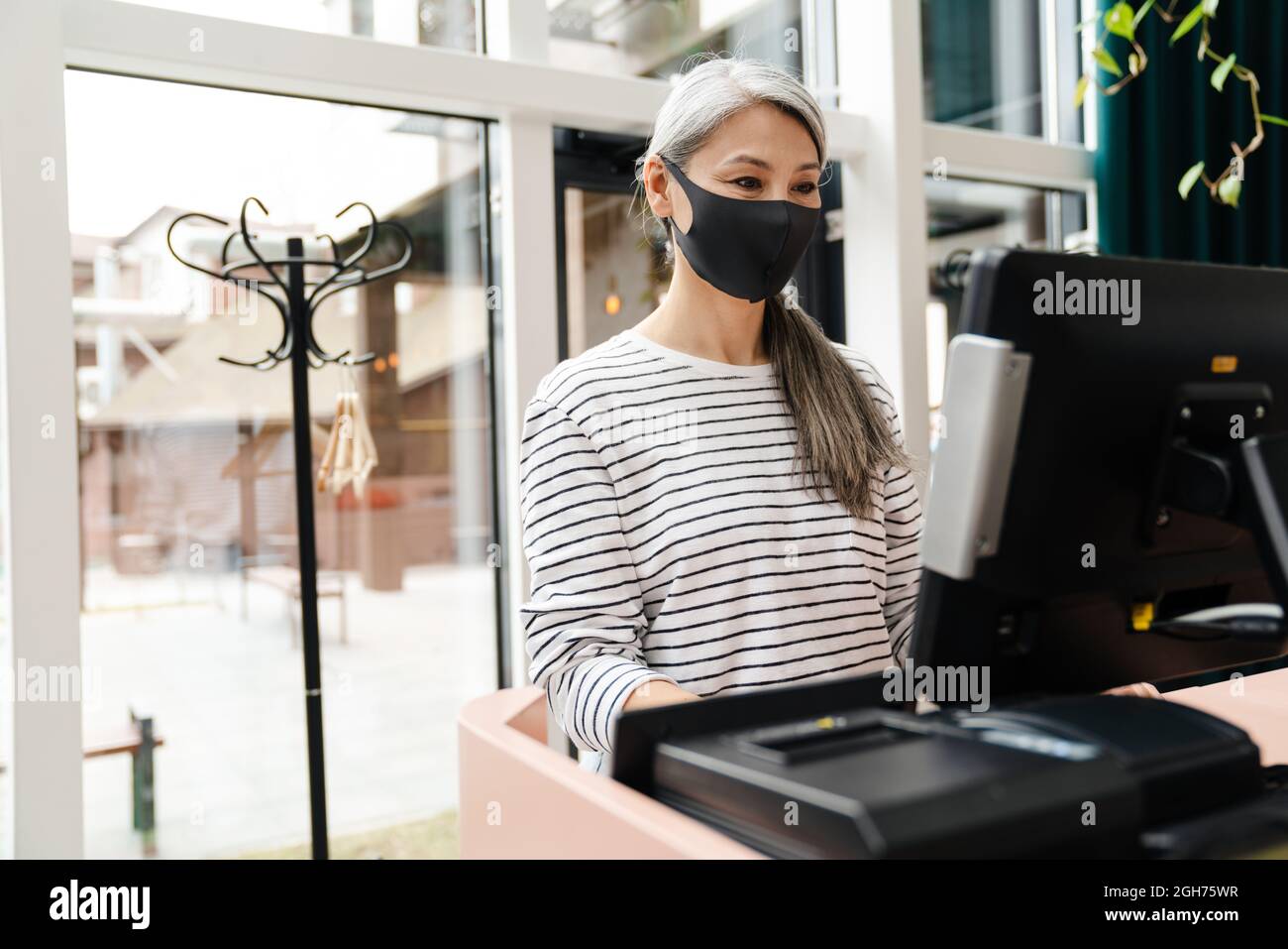 Mature waitress woman wearing face mask standing at her workplace in ...