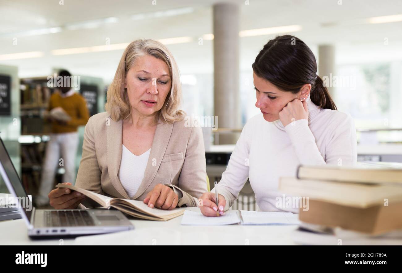 Friendly female tutor helping to diligent positive girl preparing for ...