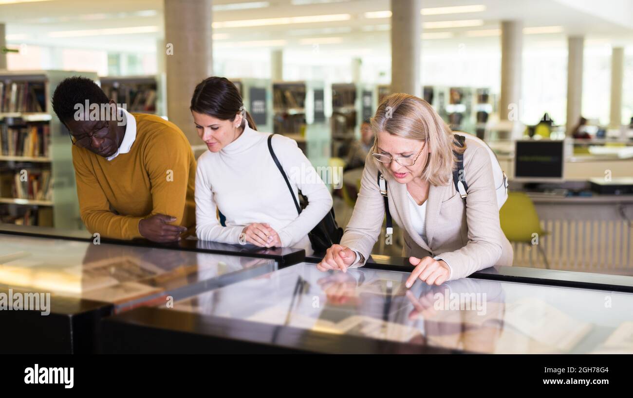 Professor and adult students read ancient books in a library showcase ...