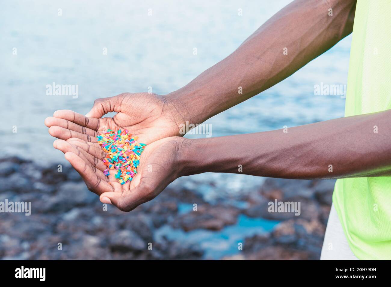 Hands full of microplastics on the beach. Different plastic colored ...