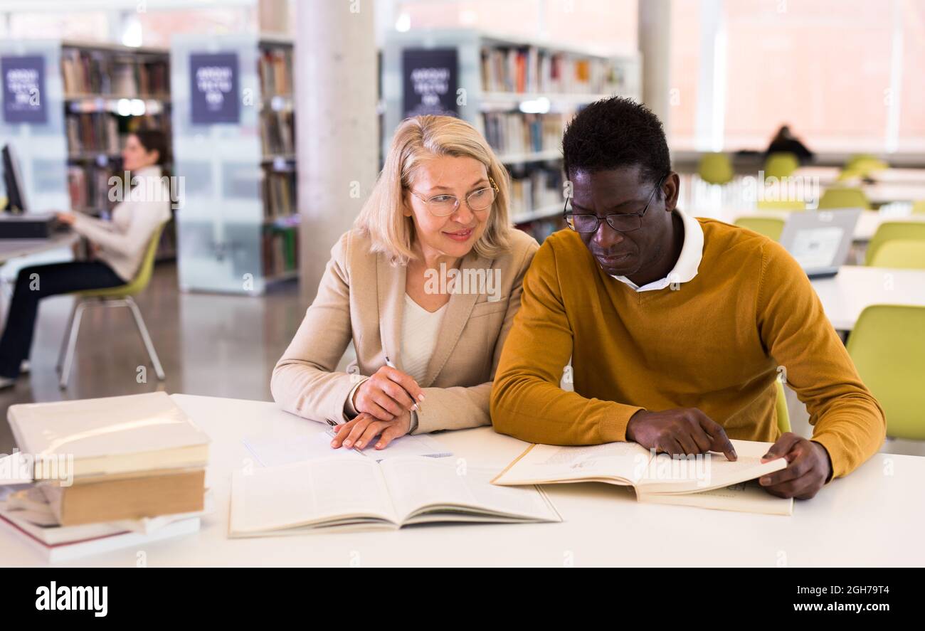 Two adult students studying together in public library Stock Photo - Alamy