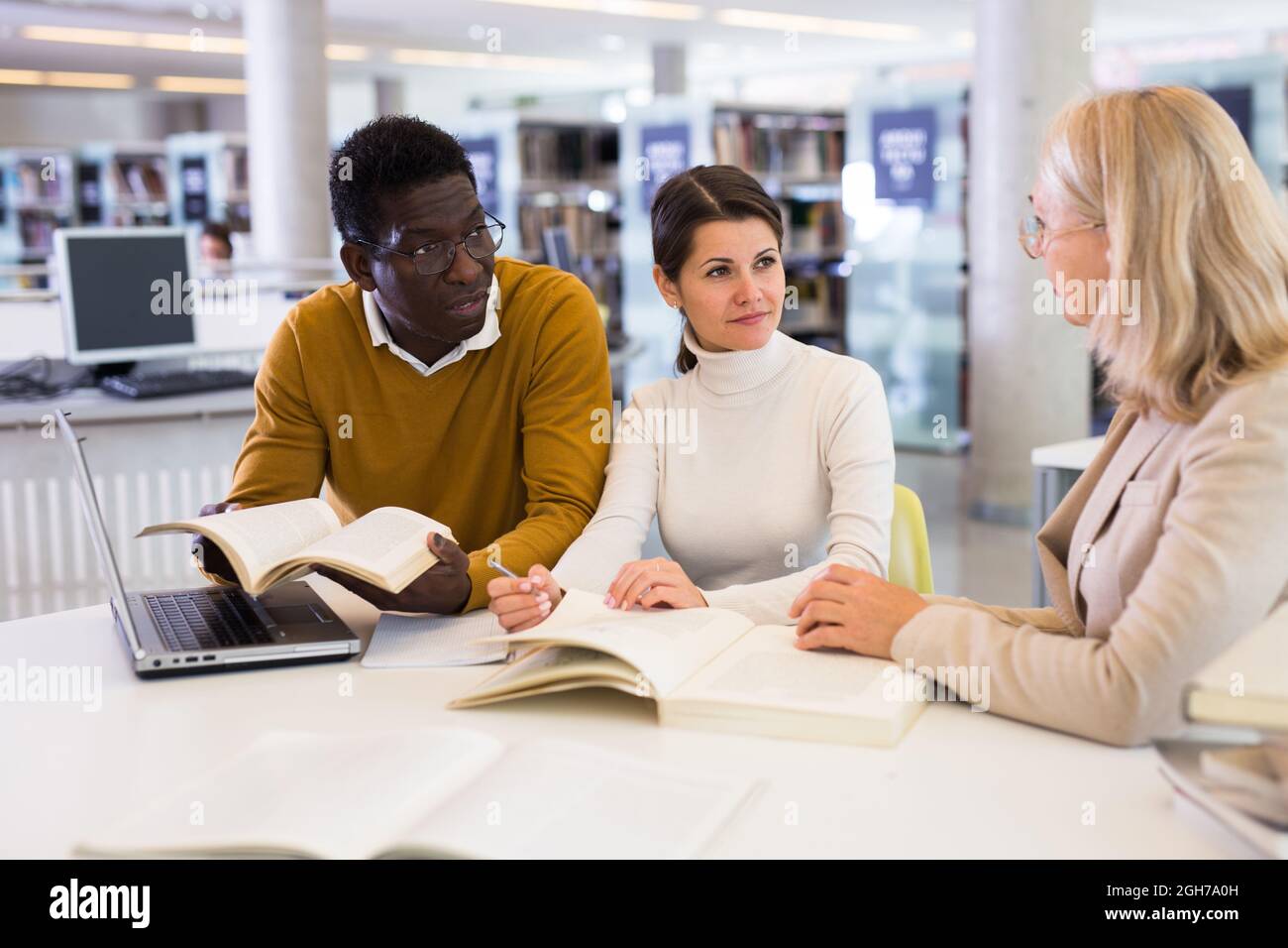 Female tutor helping students preparing for exam in library Stock Photo ...