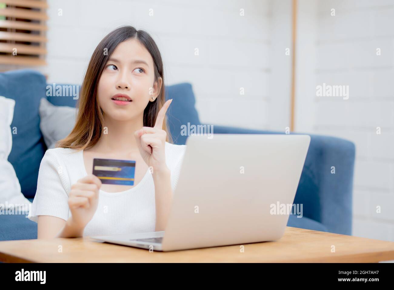 Young asian woman sitting thinking idea using credit card with laptop computer on couch, girl ...