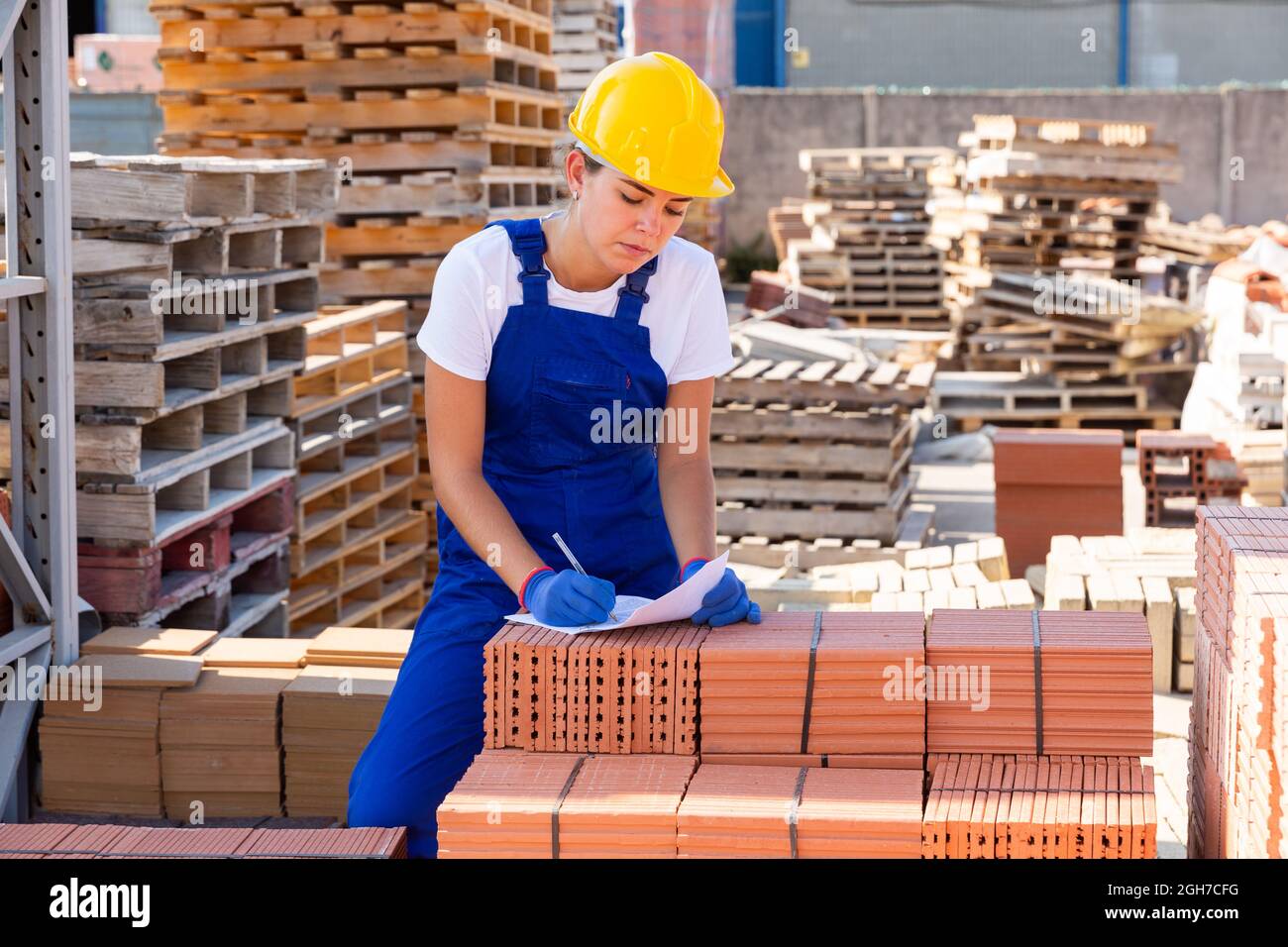 Young female worker writing beside brick stacks Stock Photo - Alamy