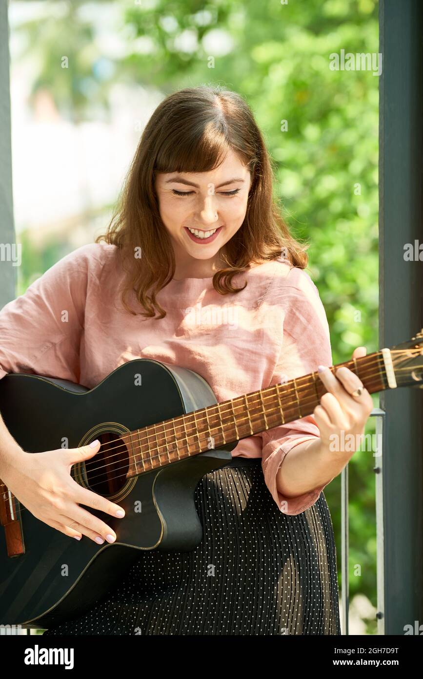 Joyful talented young woman enjoying playing guitar and singing when ...