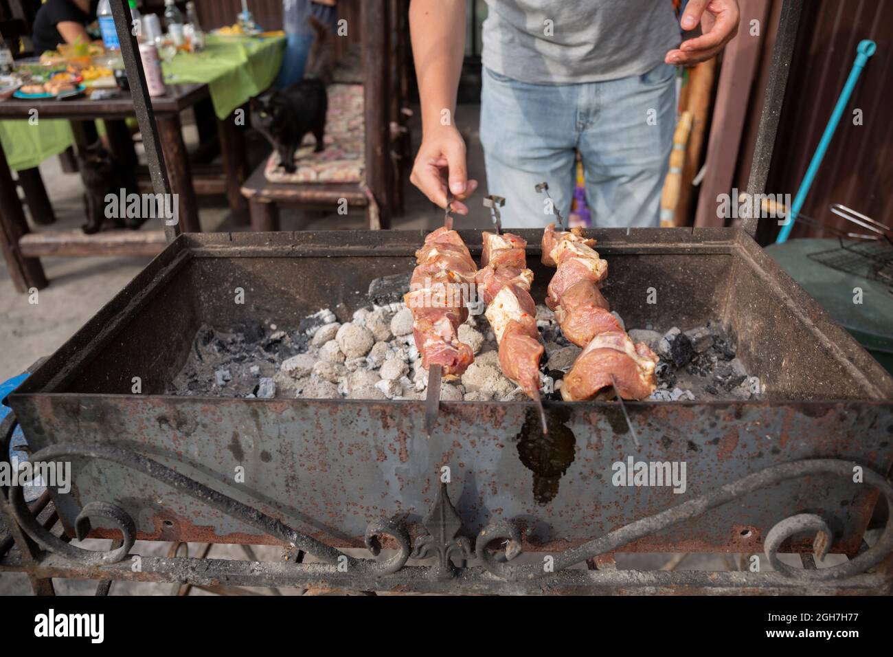 A man grills meat kebabs on an open fire on a summer day in the ...