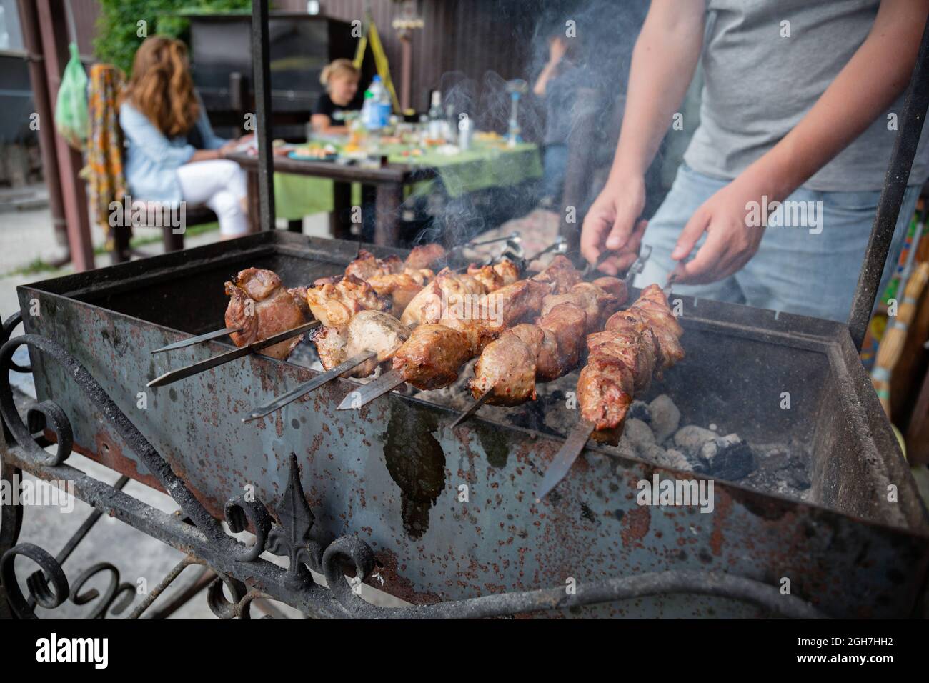 A man grills meat kebabs on an open fire on a summer day in the ...