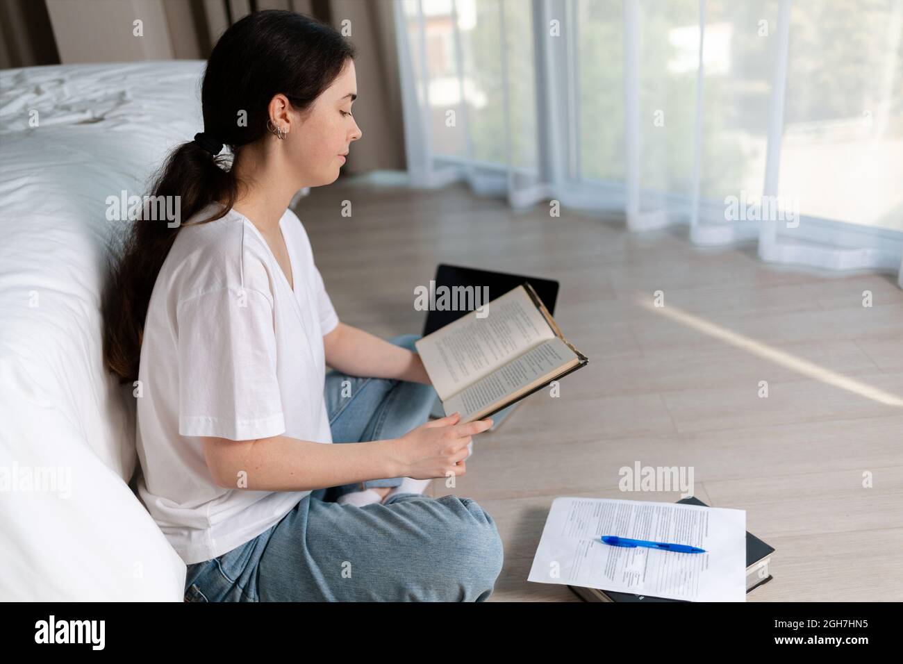 A young woman is sitting cross-legged on the floor, reading a book ...