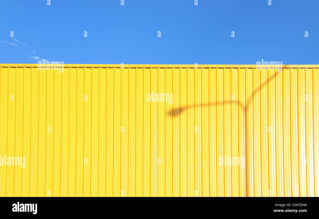 a bright yellow metal wall reflecting the afternoon sun with a shadow ...