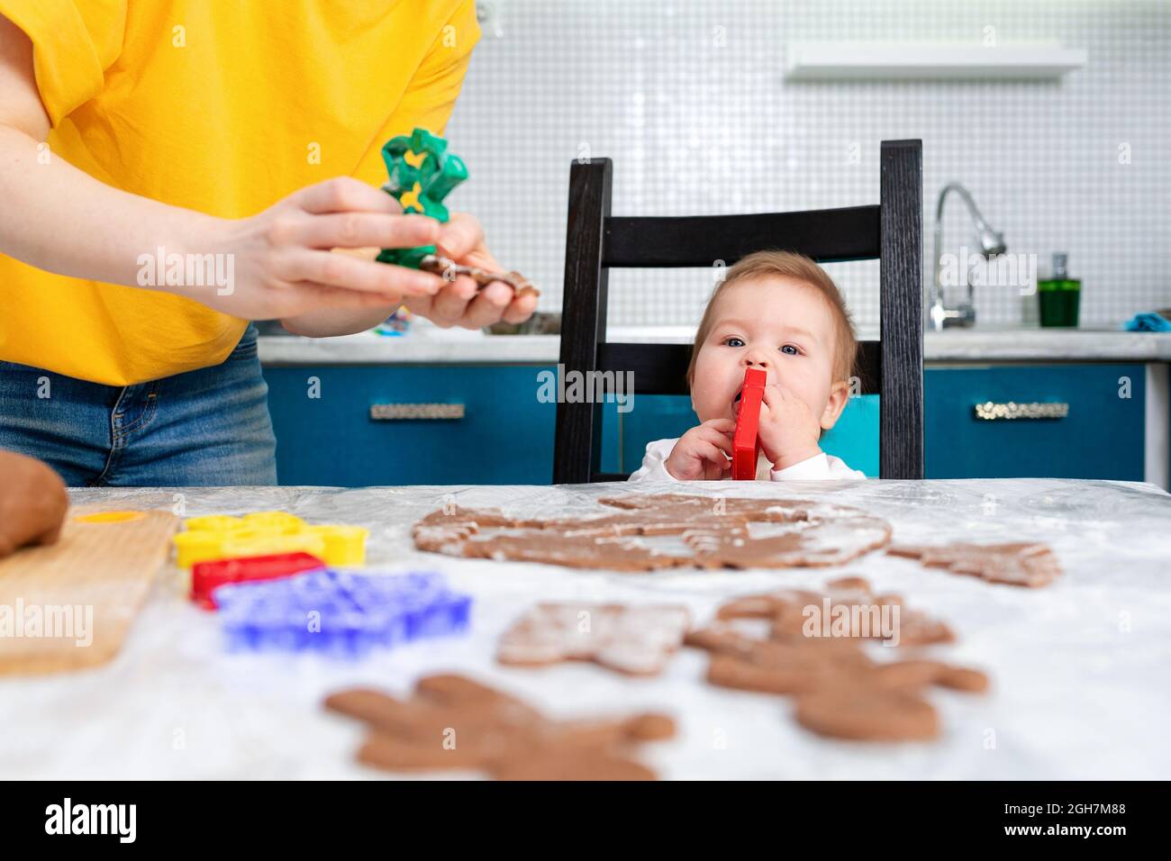 Portrait of a child chewing a cookie cutter. Mother makes gingerbread ...