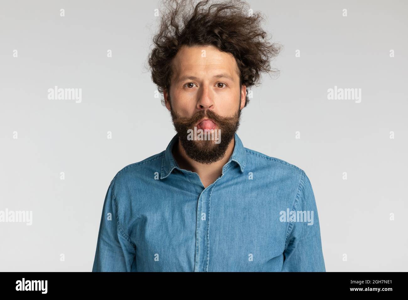 goofy young bearded man in denim shirt sticking out tongue and making ...