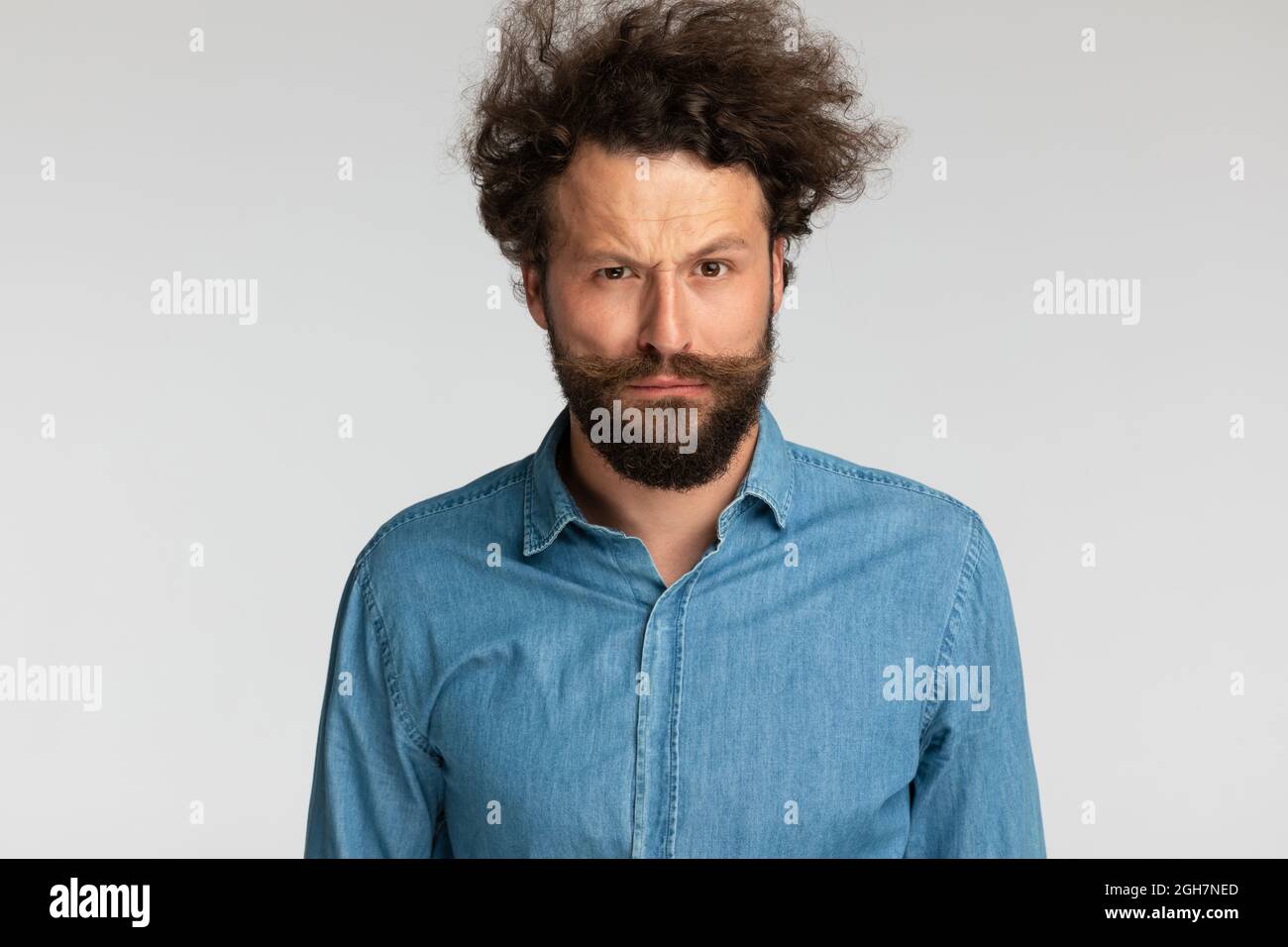 serious bearded fashion model in denim shirt frowning and posing on ...