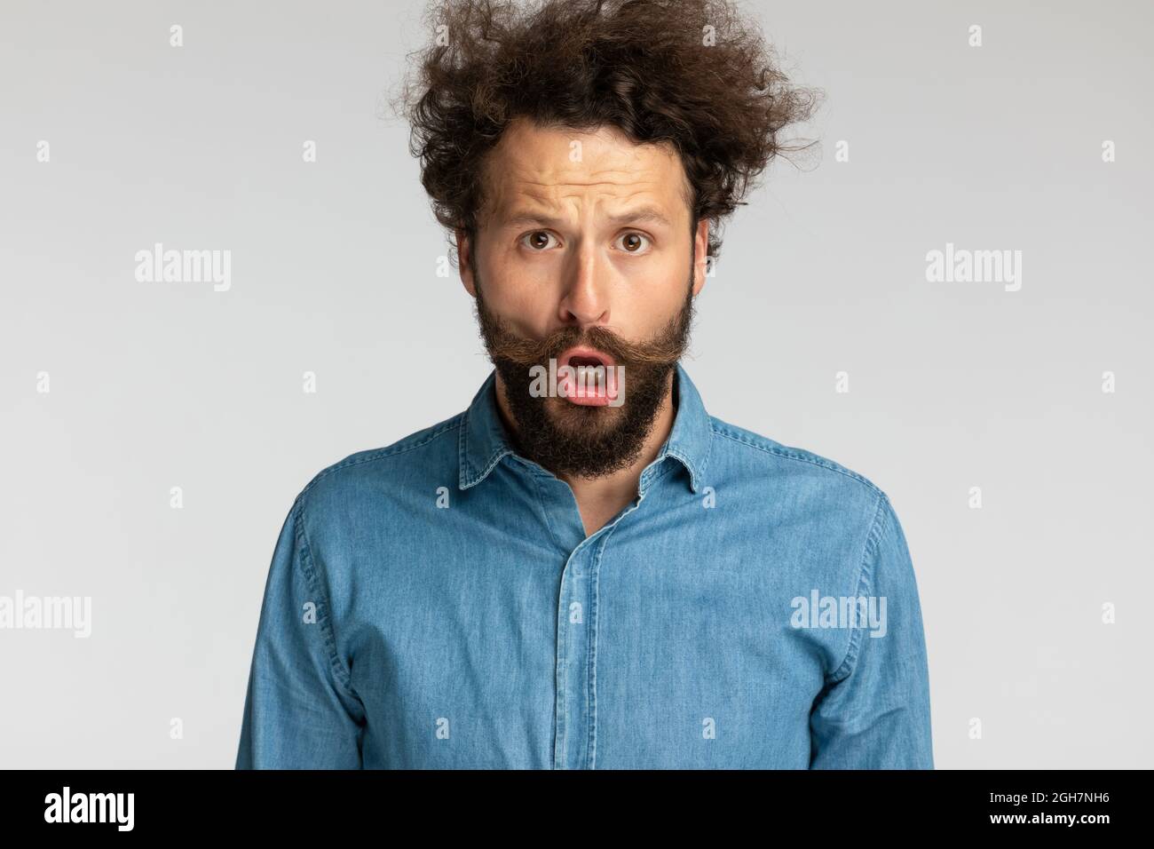 portrait of shocked young man in denim shirt opening mouth and making ...