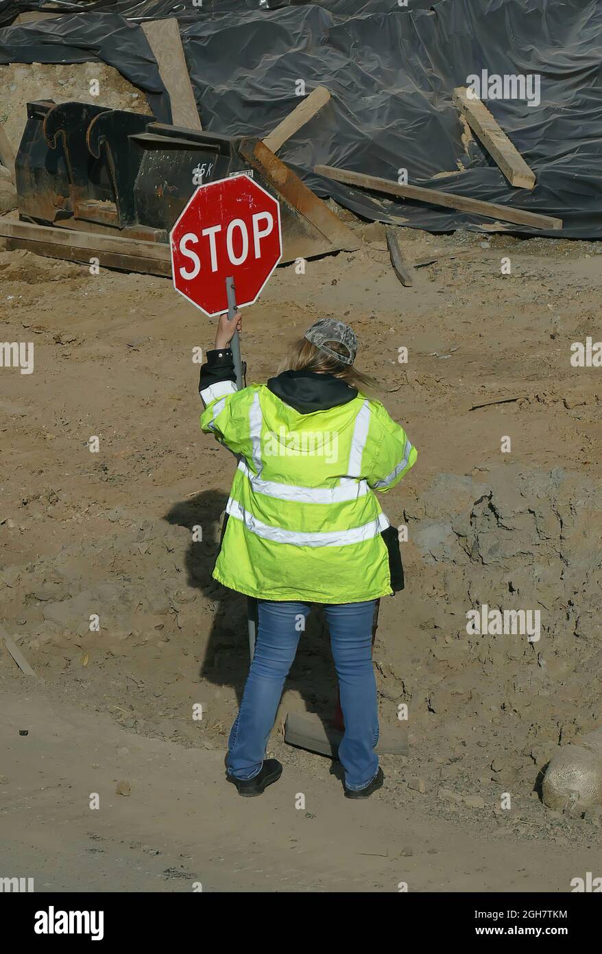 Back view of a female construction worker holding the metal "STOP" sign ...