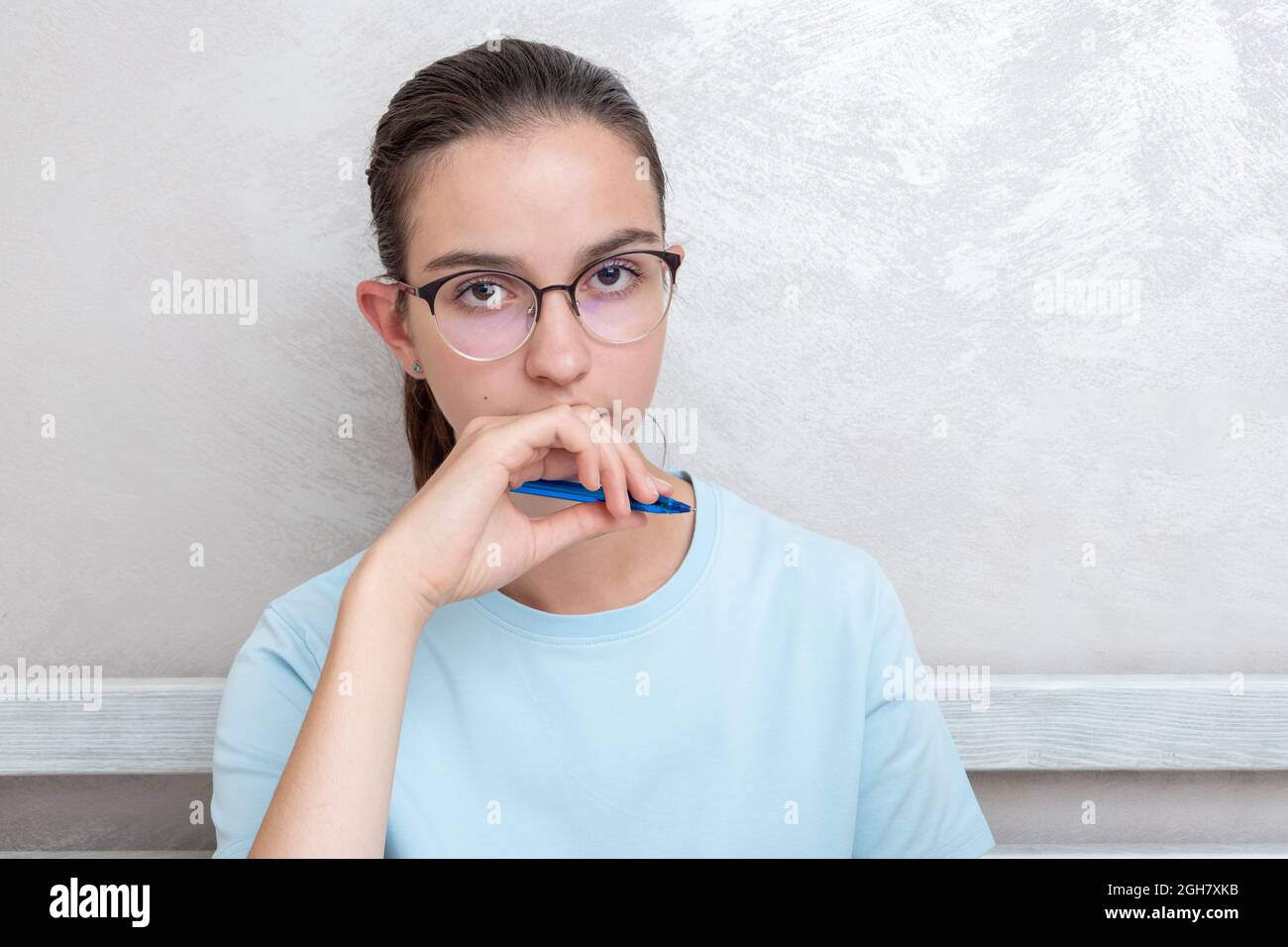 Pensive attractive female student holding pen in mouth and looking at ...