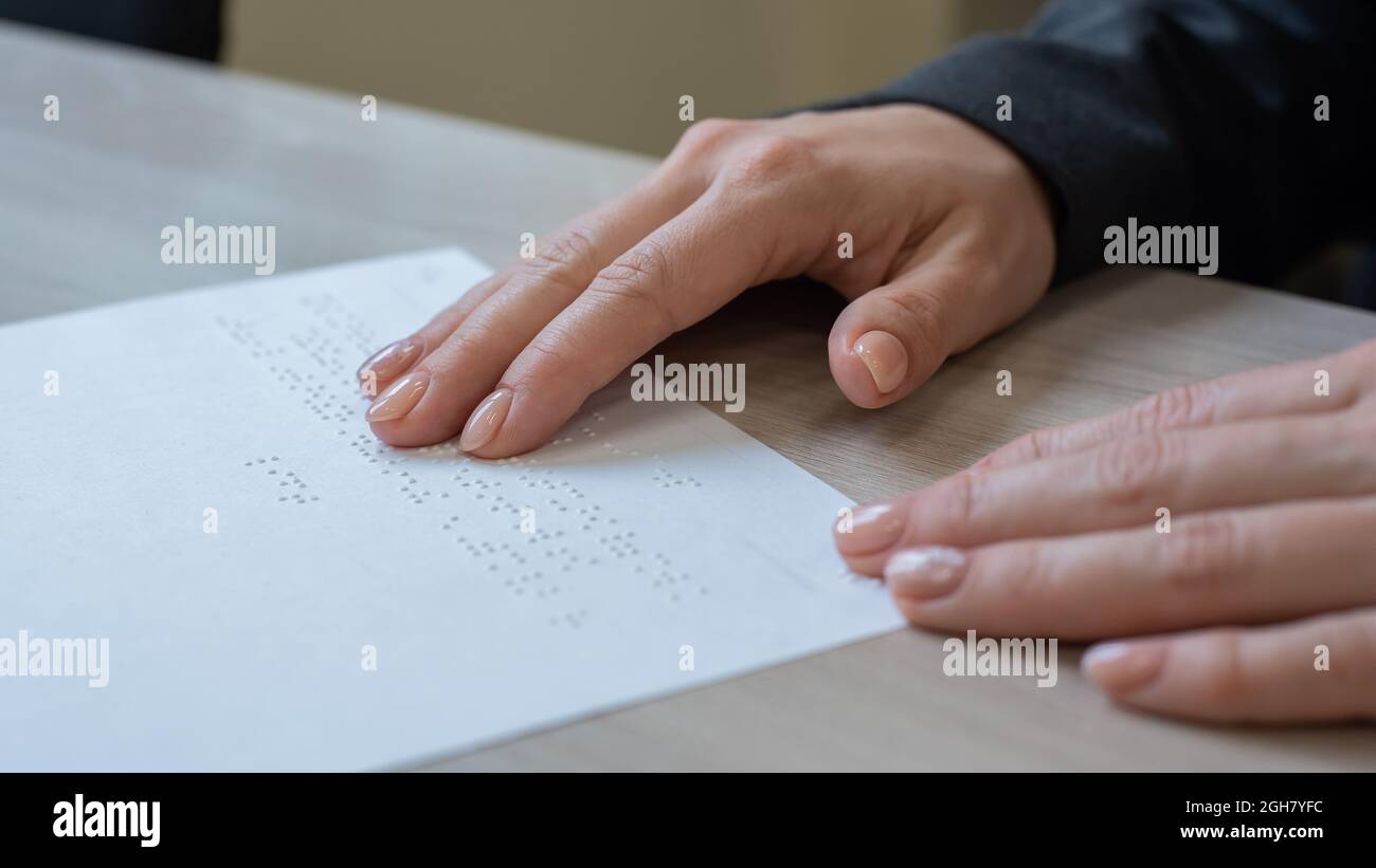 Close-up woman reads the text to the blind. Woman's hands on paper with ...