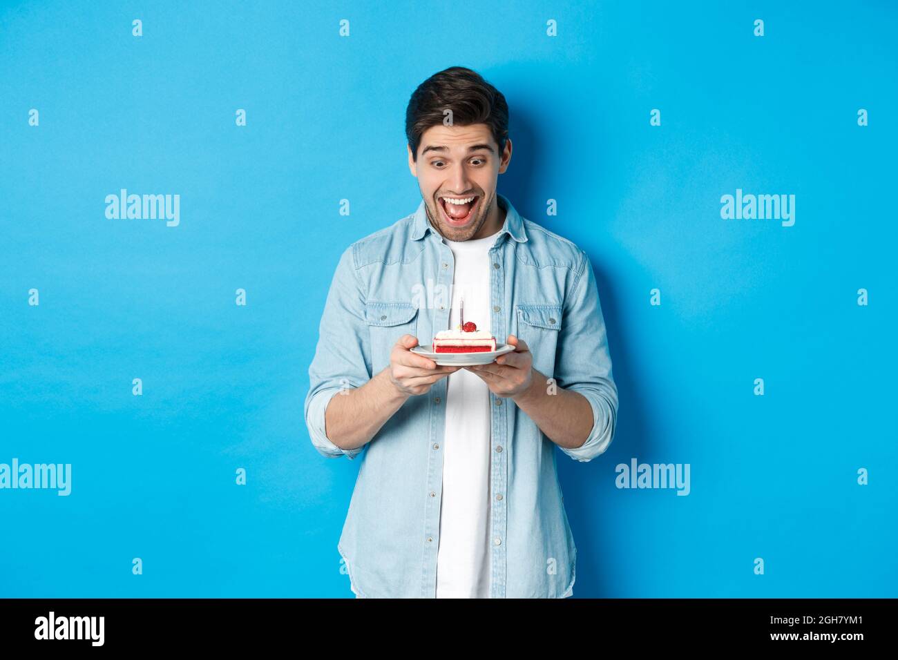 Excited young male model looking at birthday cake and smiling, making a ...