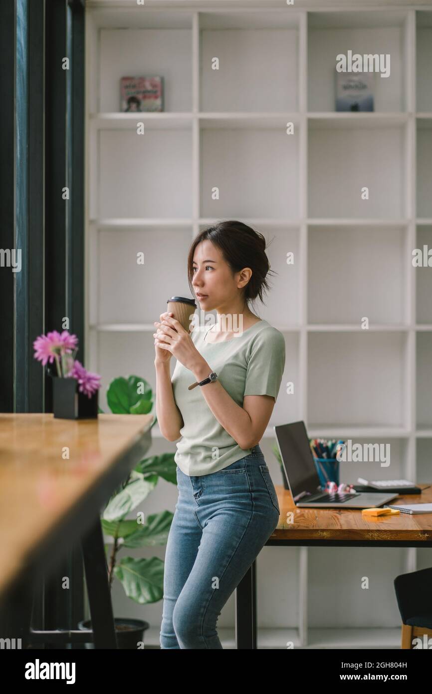 Asian woman standing on front of office workplace while hand holding a ...