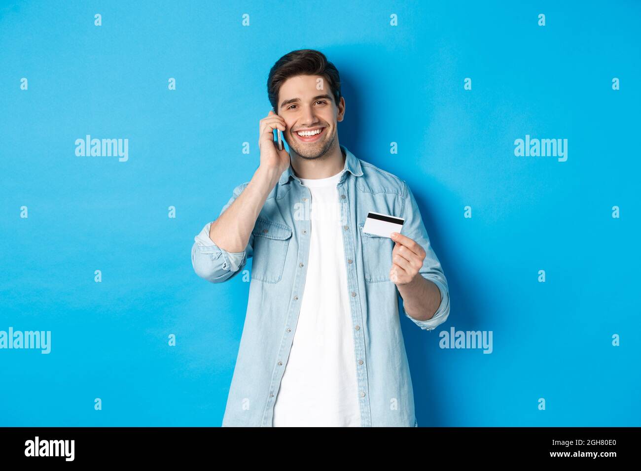 Handsome man calling bank and holding credit card, having mobile ...