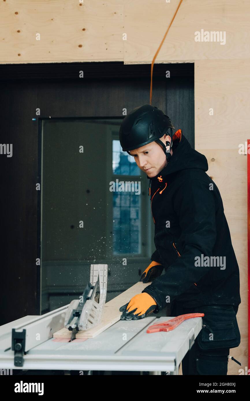 Male worker using table saw for cutting wooden plank while working at ...