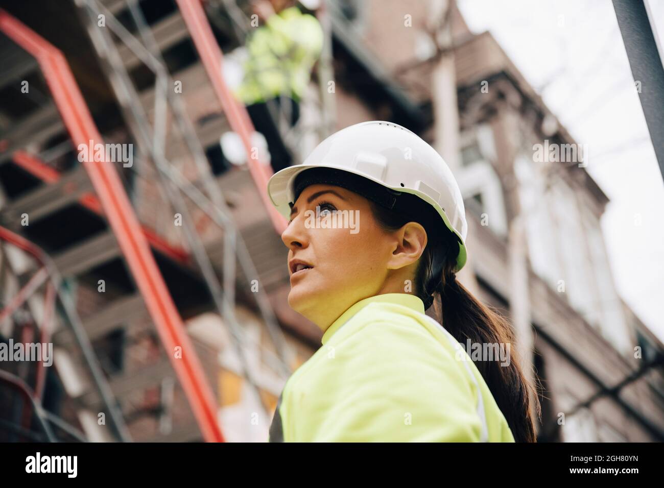 Female building contractor in hardhat looking away at construction site ...