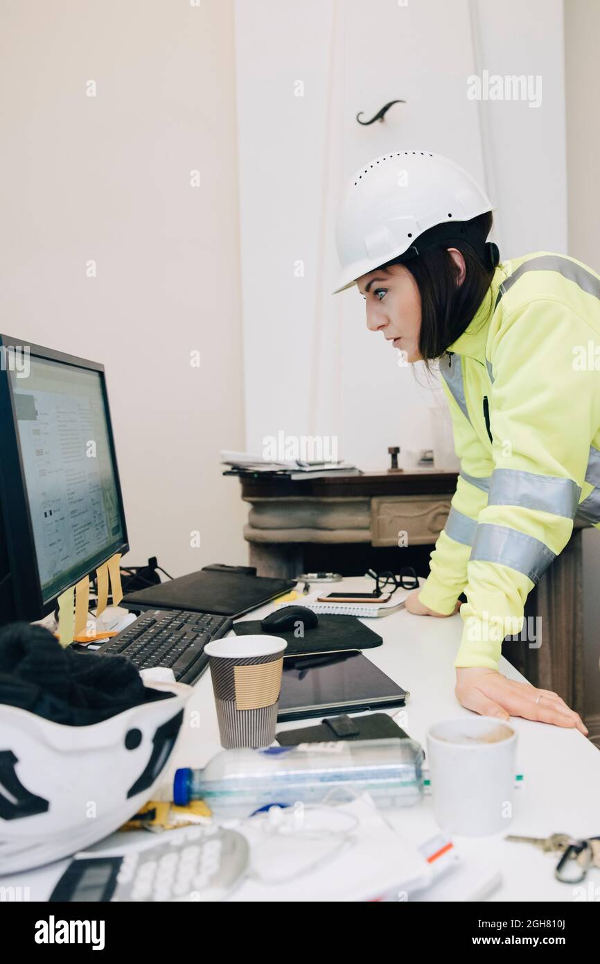 Female building contractor in hardhat using computer while leaning on ...
