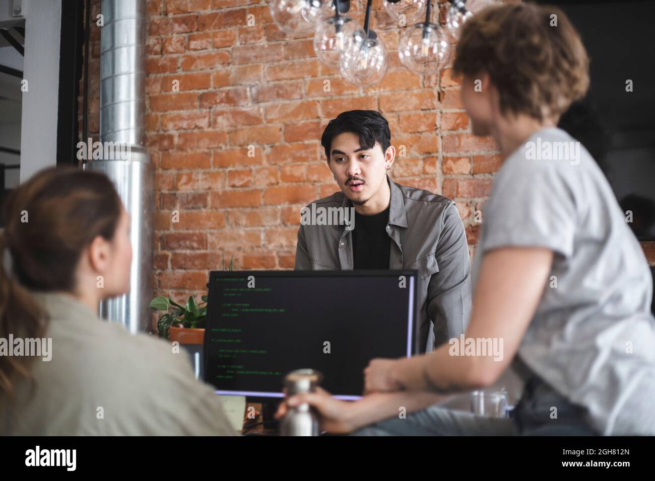 Male computer programmer discussing with female colleagues in office ...