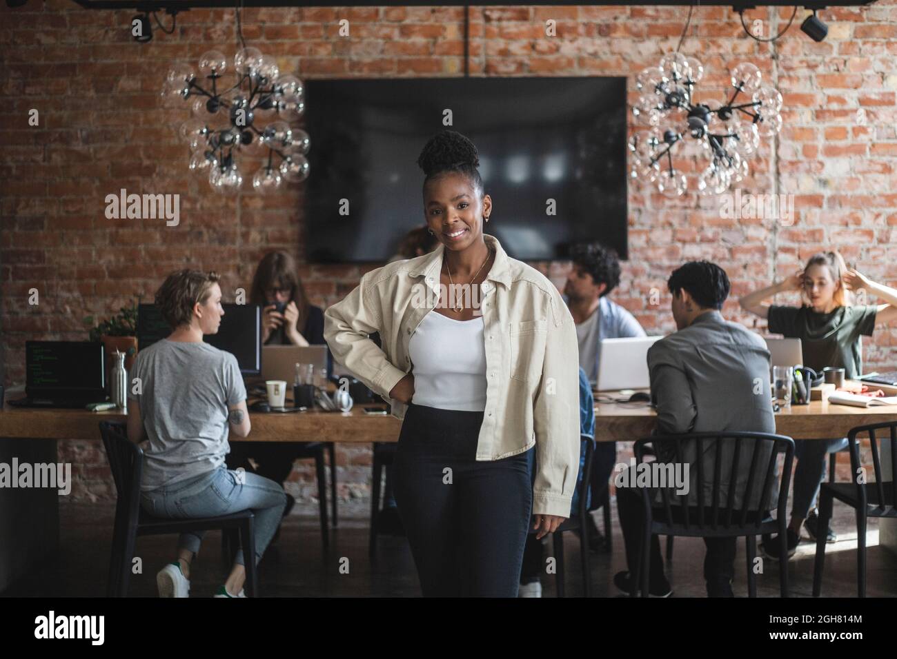Female entrepreneur standing with arms crossed while colleagues working ...