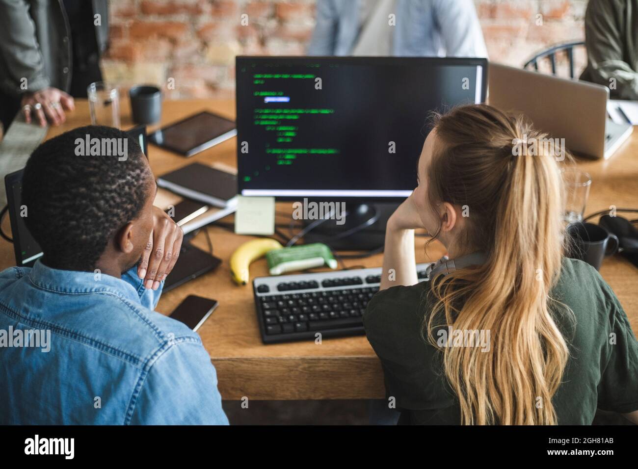Rear view of male and female colleagues coding over computer at startup ...