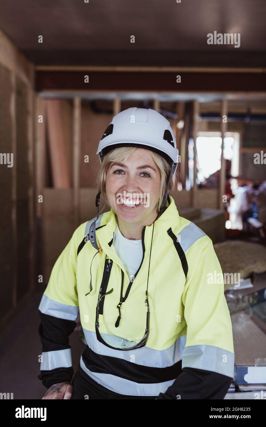 Cheerful female building contractor wearing hard hat sitting at ...