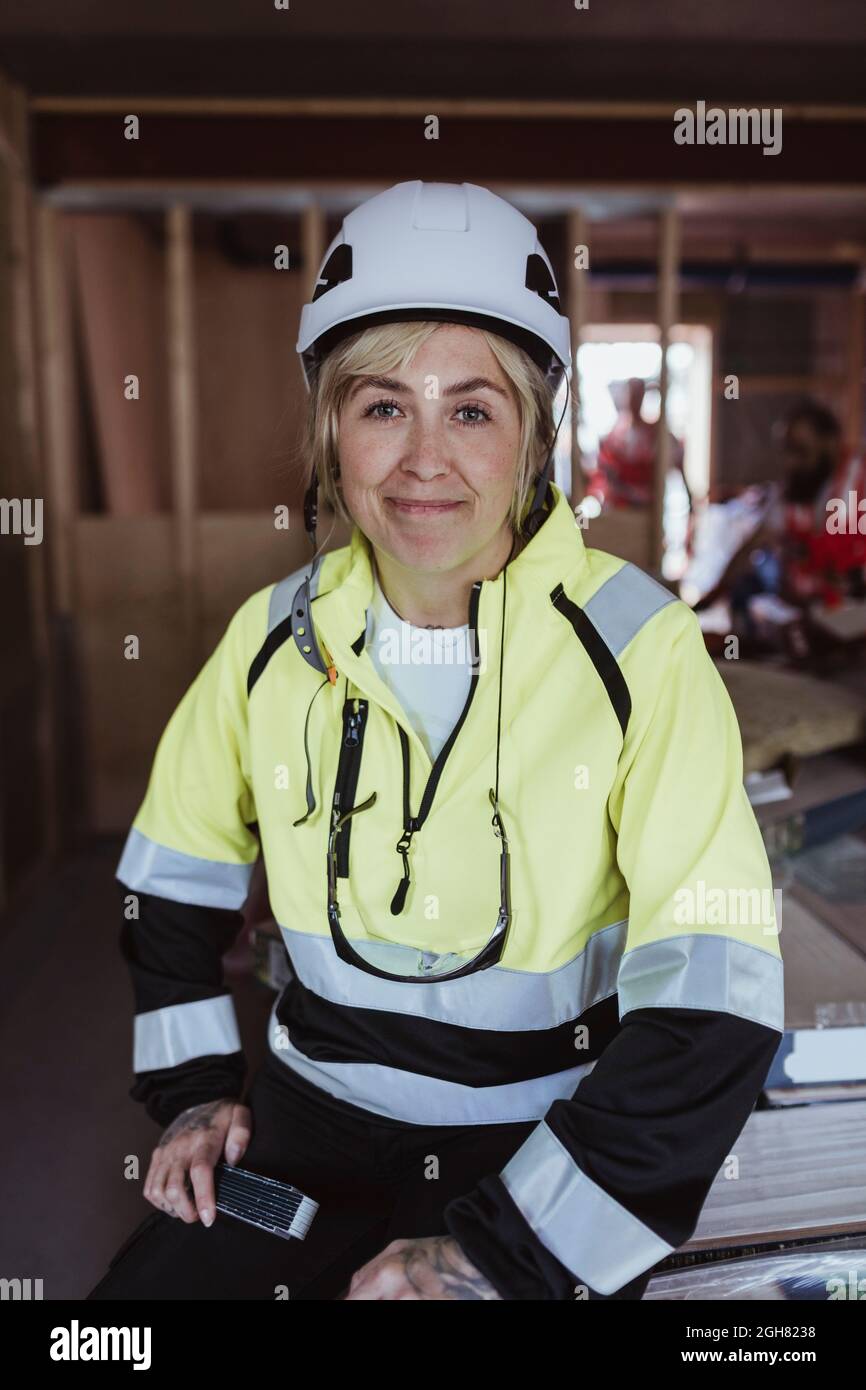 Smiling female building contractor wearing hard hat sitting at ...