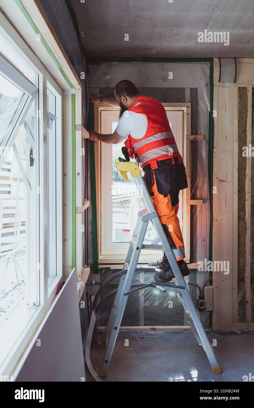 Full length of male construction worker standing on step ladder working ...
